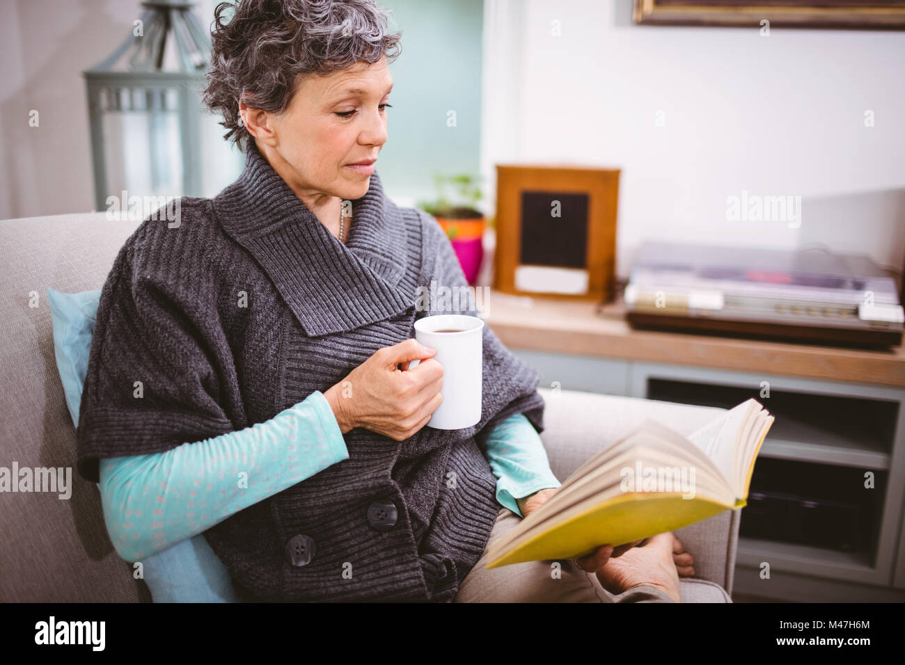 Mature woman reading book and holding coffee mug Stock Photo - Alamy