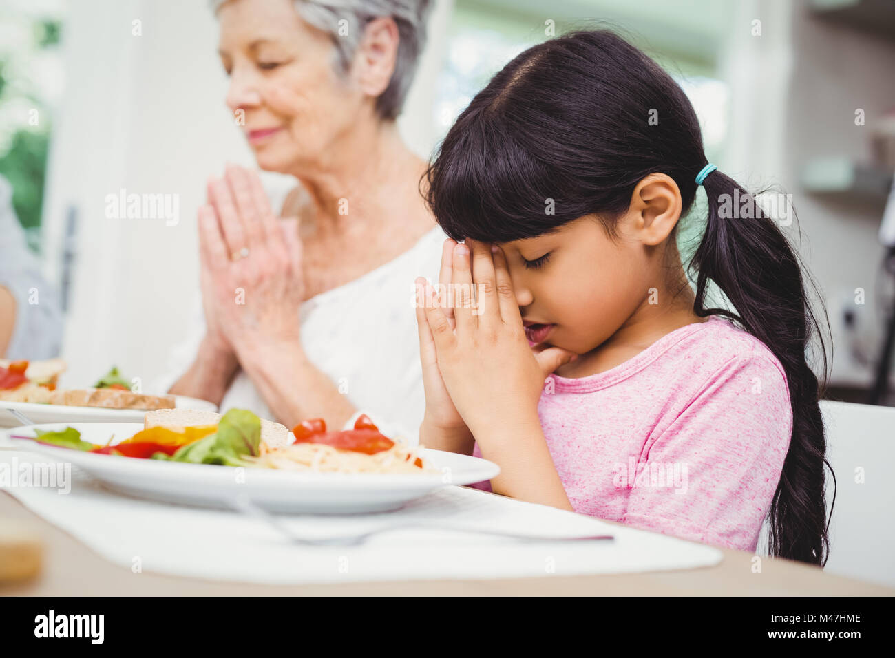 Granny and granddaughter praying at dining table Stock Photo - Alamy