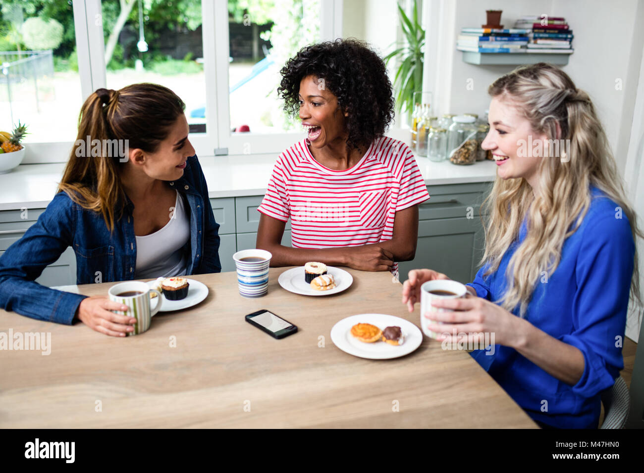 Female friends laughing while having breakfast Stock Photo - Alamy