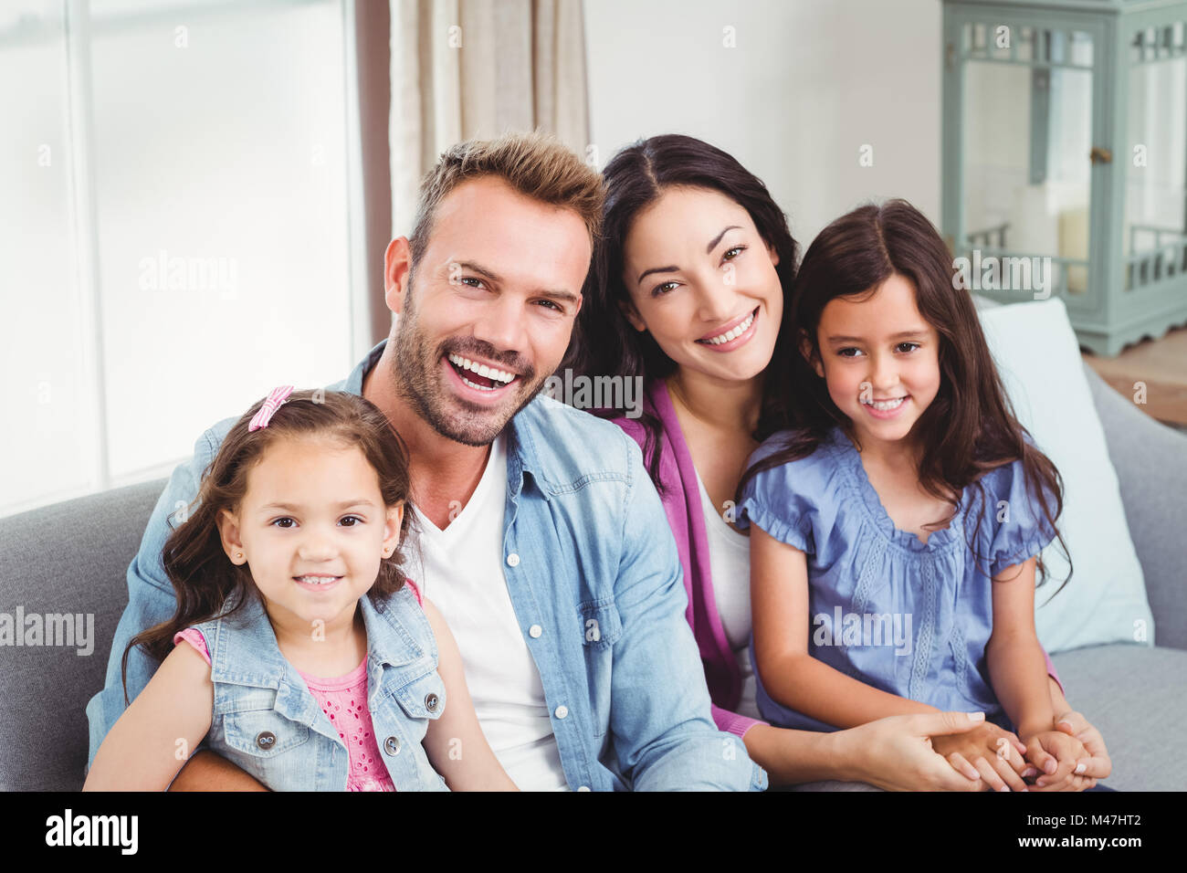 Parents smiling while sitting with daughters on sofa Stock Photo - Alamy