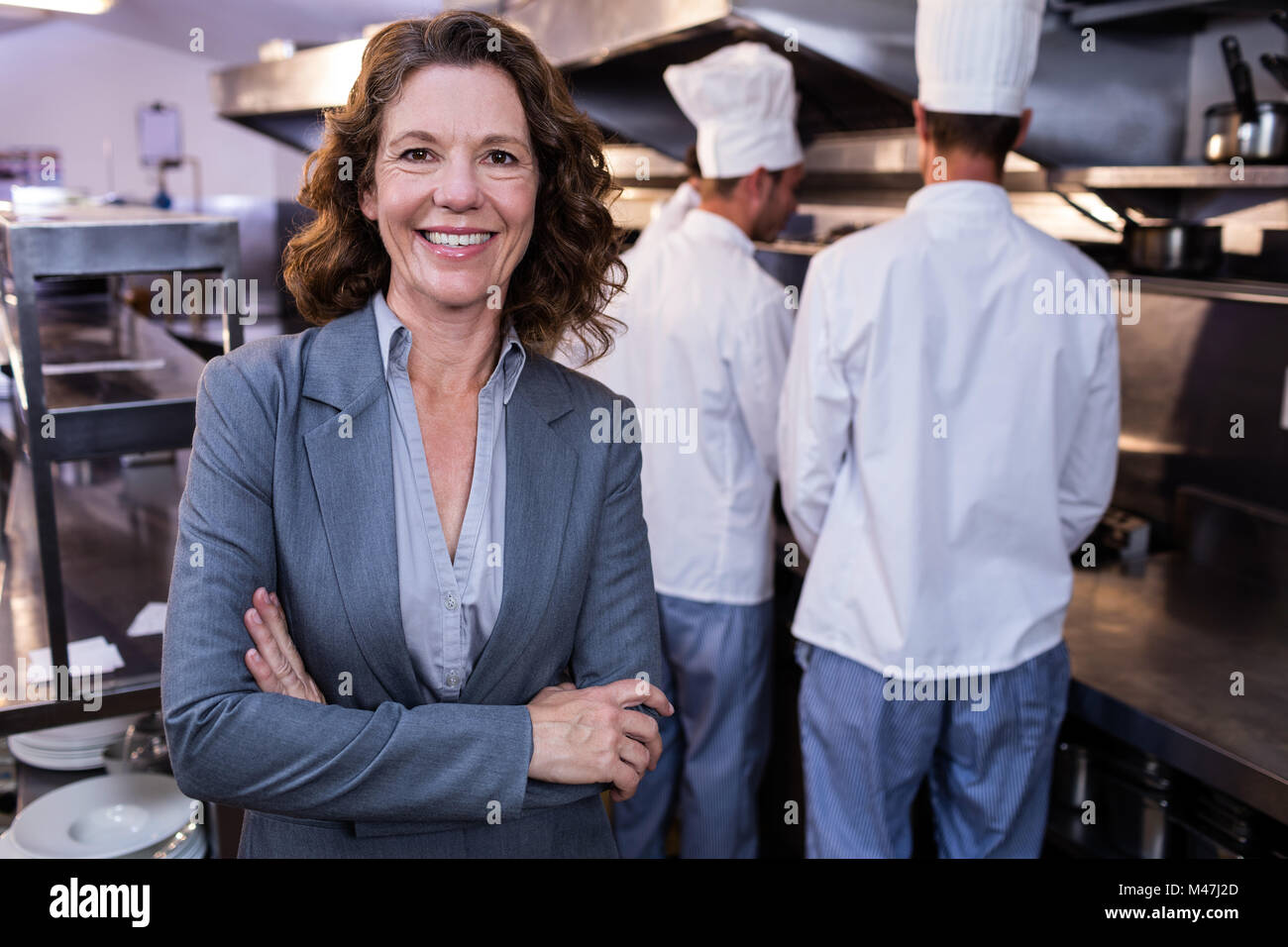 Happy restaurant manager standing with arms crossed in commercial ...