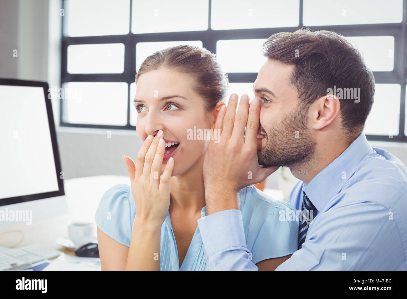 Happy businessman whispering to female colleague Stock Photo - Alamy