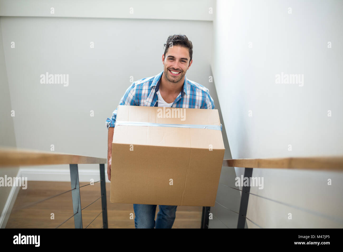 Portrait of smiling man holding cardboard box while climbing steps ...