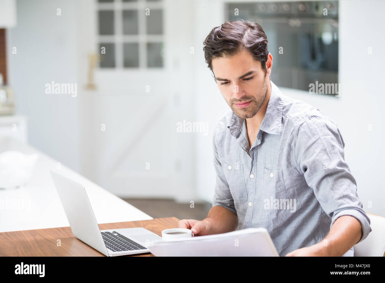 Young man reading documents while sitting at desk with laptop Stock ...