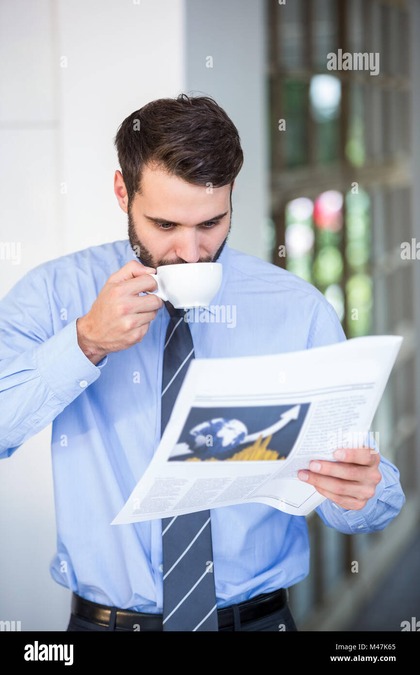 Businessman drinking coffee while reading newspaper Stock Photo - Alamy