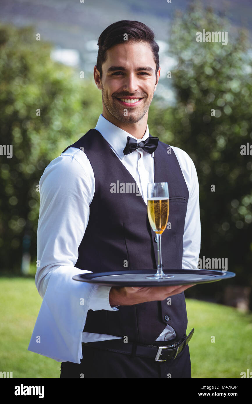 Handsome waiter holding a tray with glass of champagne Stock Photo - Alamy