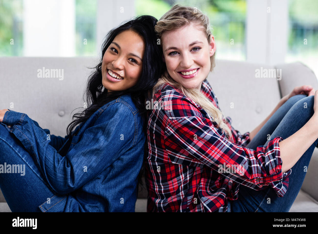 Happy beautiful female friends sitting back to back Stock Photo - Alamy