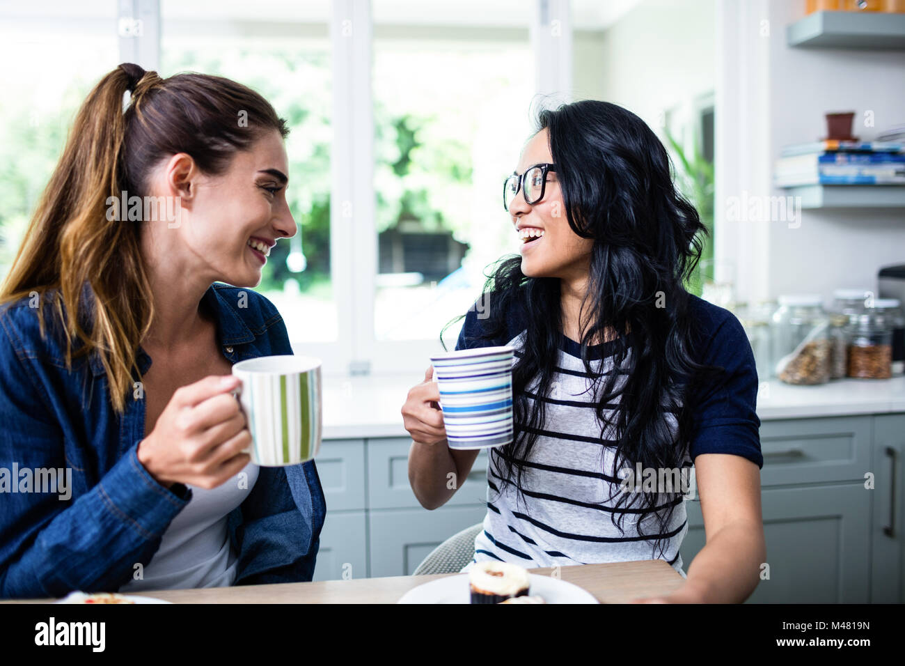 Young female friends laughing while drinking coffee Stock Photo - Alamy