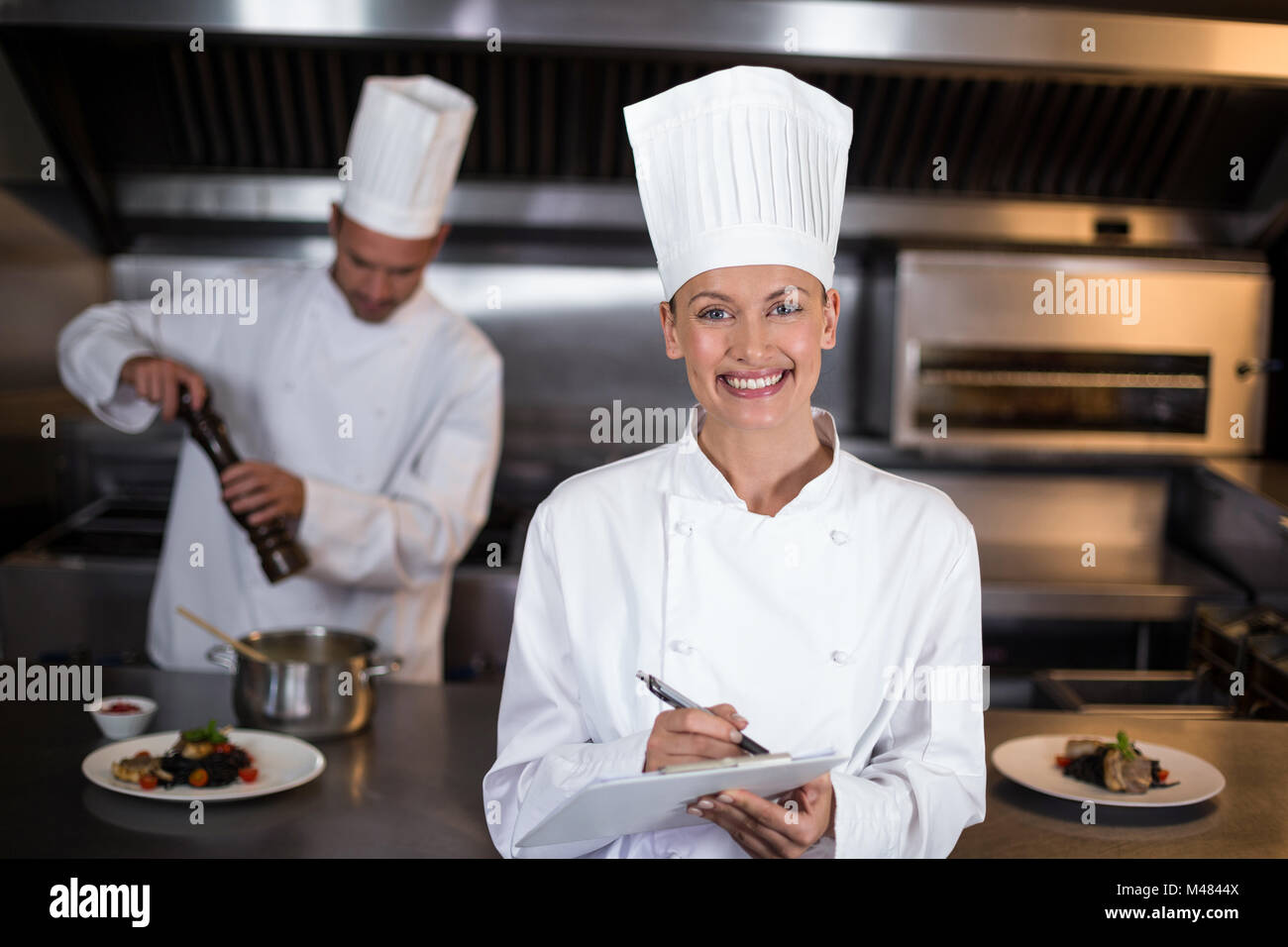 Portrait of smiling female chef writing on clipboard Stock Photo - Alamy