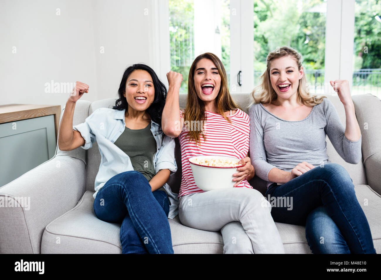 Young female friends cheering while sitting on sofa Stock Photo - Alamy