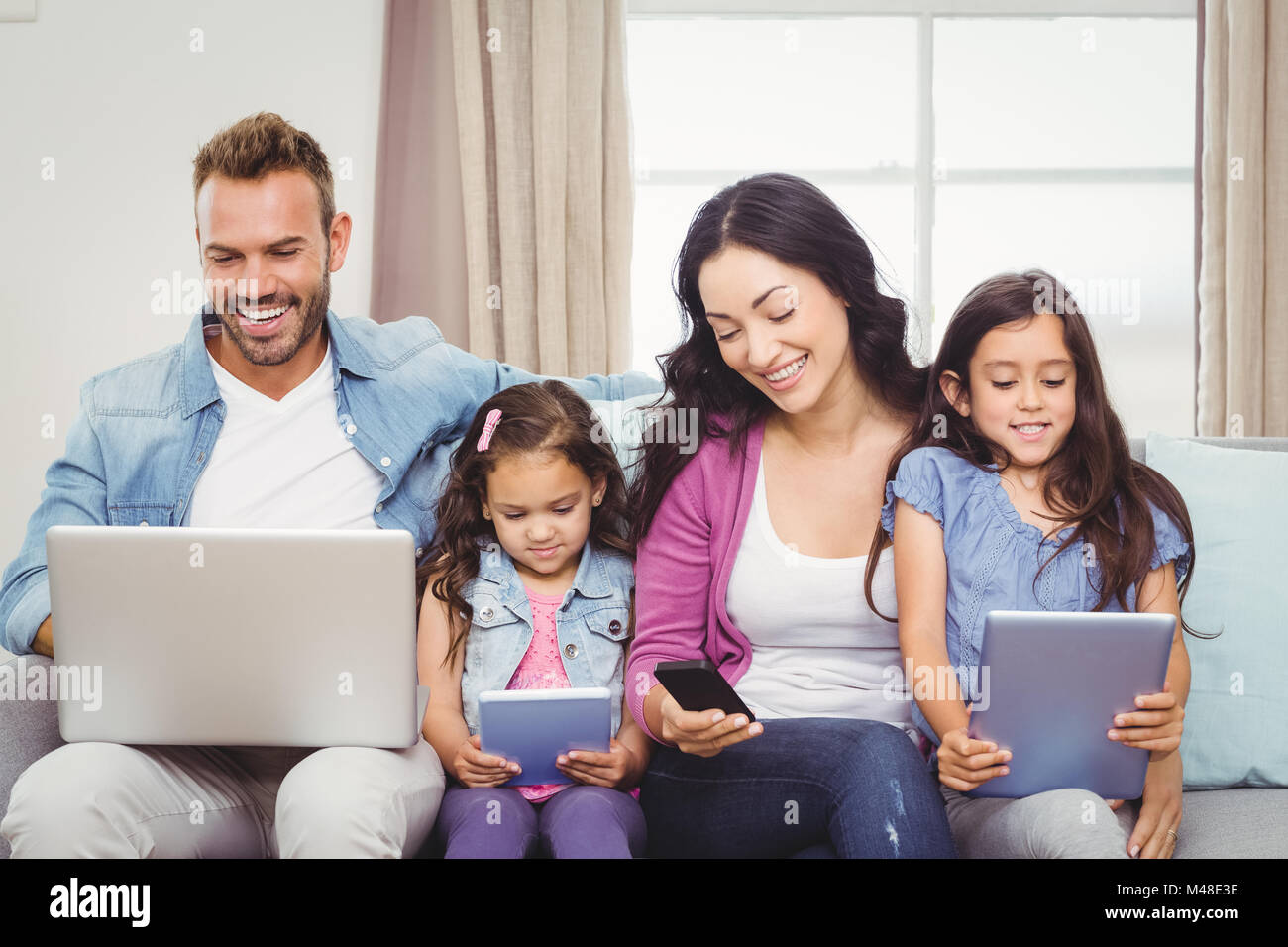Family using modern technologies while sitting on sofa Stock Photo - Alamy