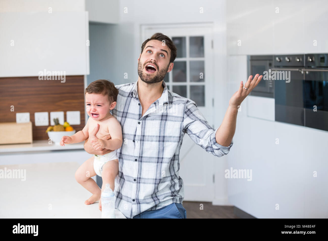 Frustrated father holding crying baby boy in kitchen Stock Photo - Alamy