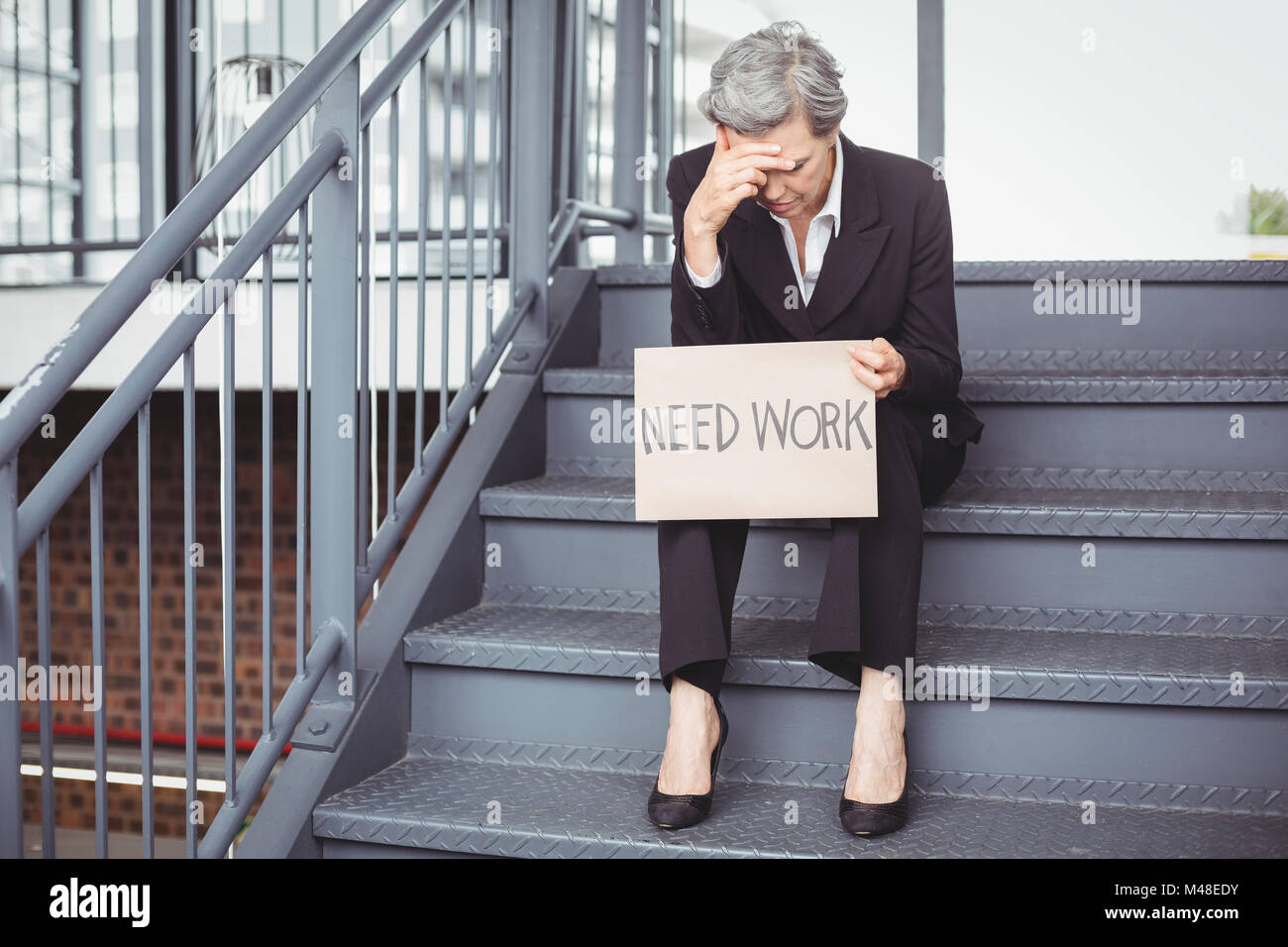 Unemployed businesswoman holding need work placard Stock Photo - Alamy