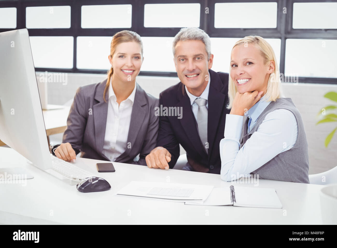 Portrait of smiling business professionals working at computer desk ...