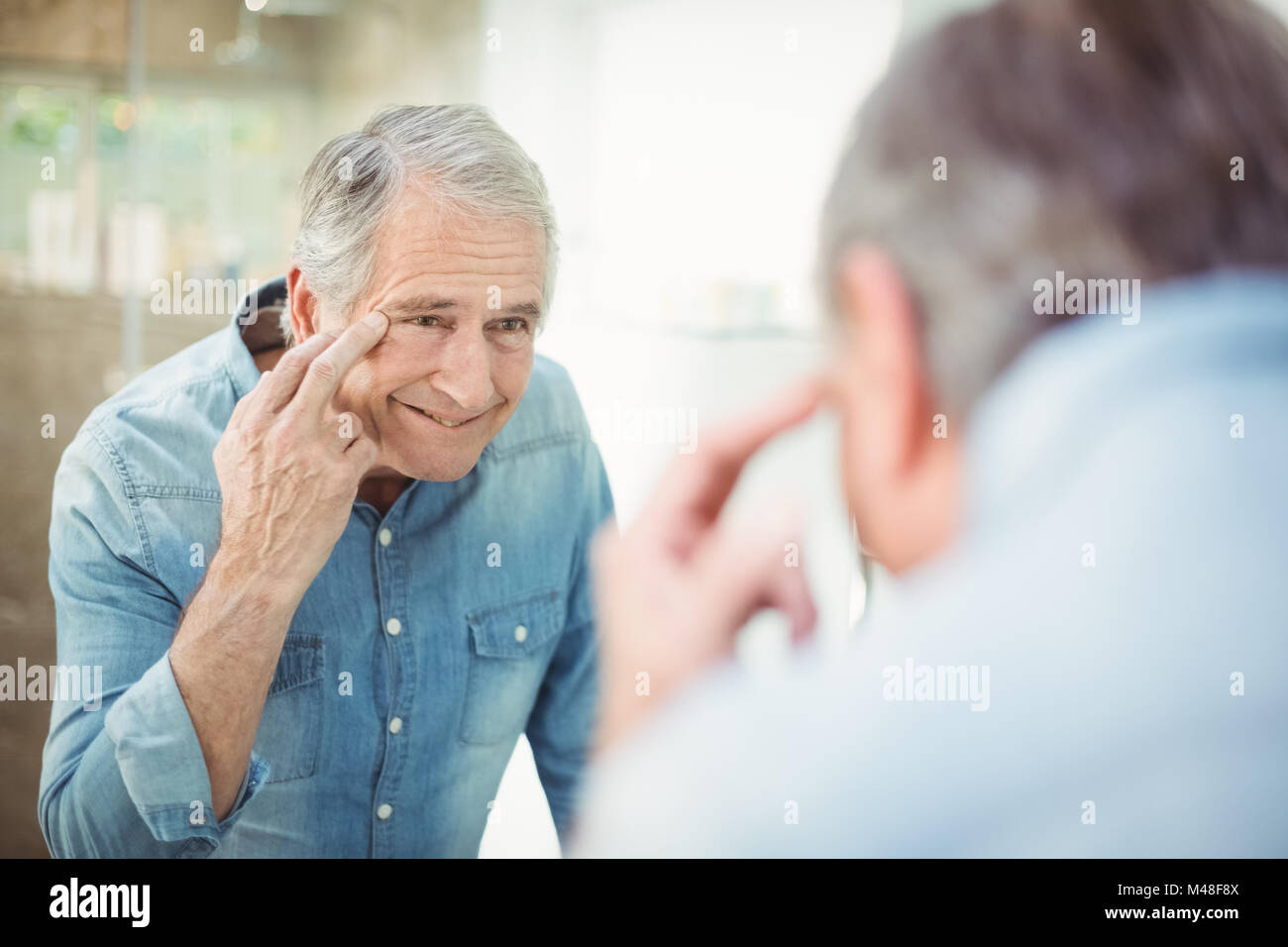 Reflection of senior man looking at skin in mirror Stock Photo - Alamy