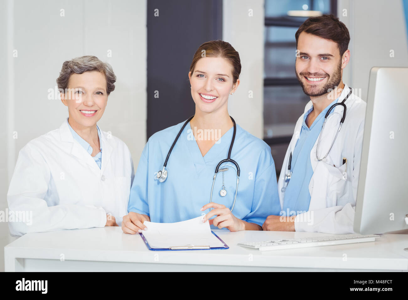 Portrait of smiling doctor team standing at computer desk Stock Photo ...