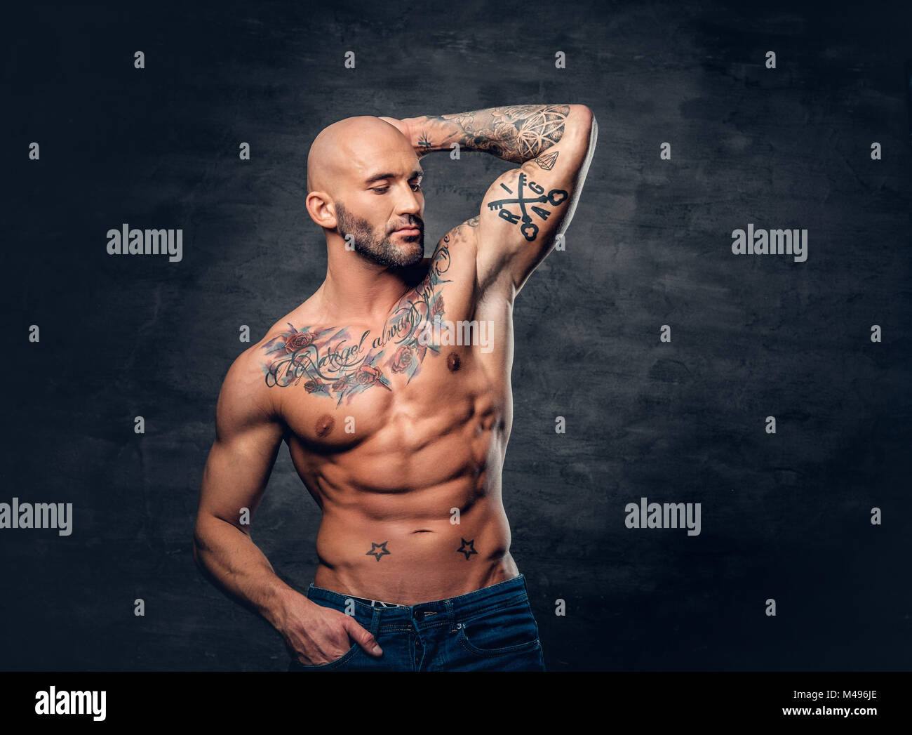 Shaved head, muscular male with tattoos on his torso over grey v Stock ...