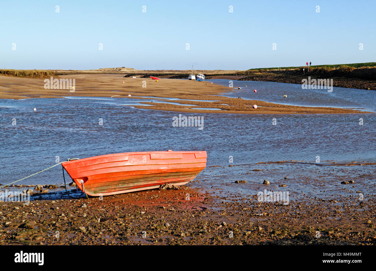 A red dinghy beached at low water on the North Norfolk coast at Burnham ...