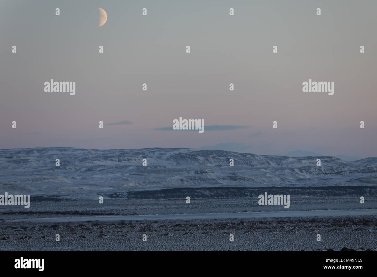 Crescent moon over a wintery, mountainous Icelandic landscape in the ...