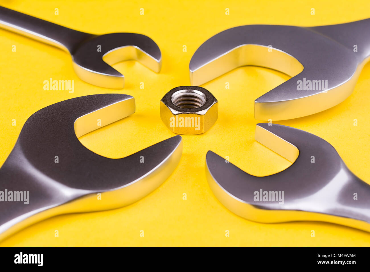 Spanners of various sizes arranged around a screw on a yellow ...