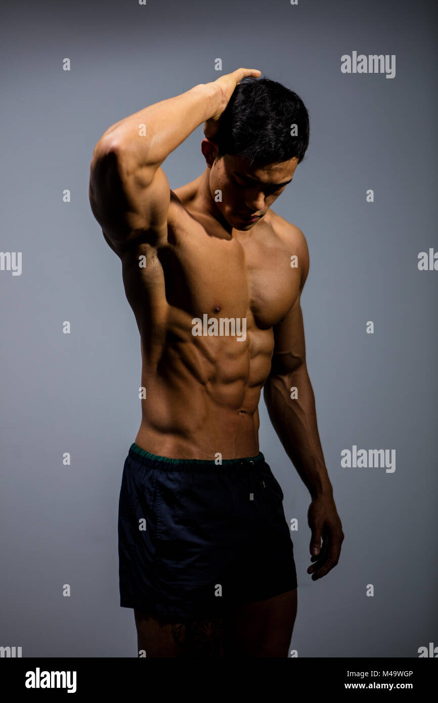 A muscular Asian fitness model flexes his muscular abdomen with an arm ...