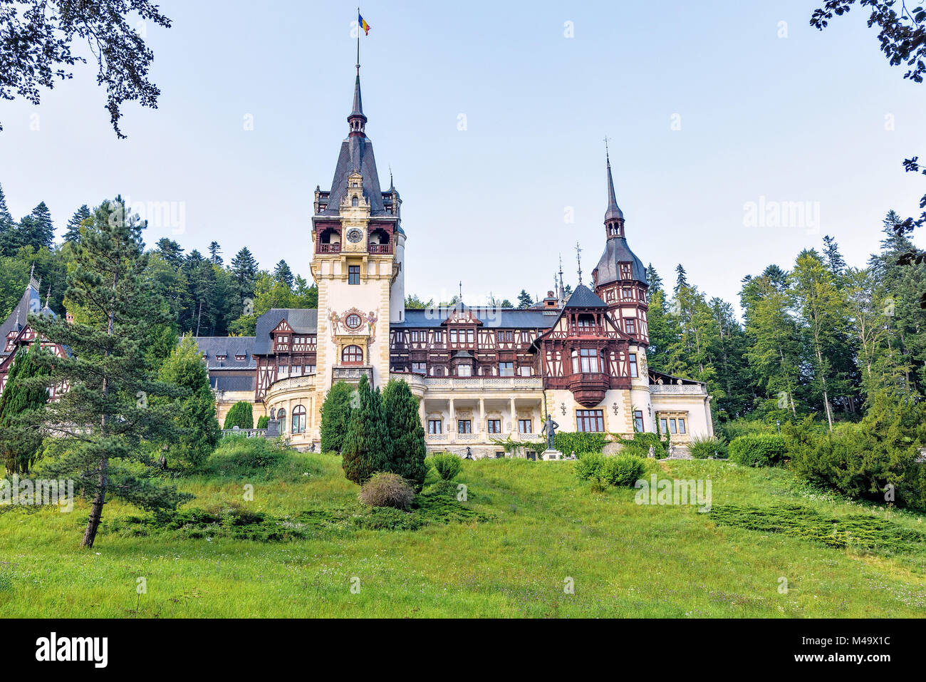 Daylight far view to Peles castle front facade with hanging flag. Tree ...