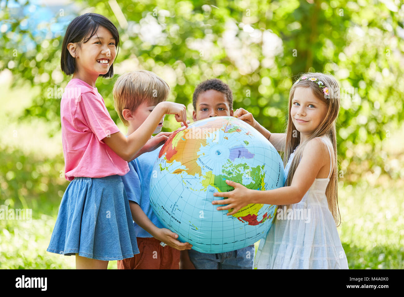 Multicultural group of children in nature is holding a world globe ...