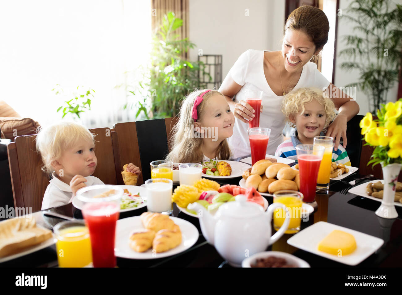 Healthy family breakfast at home. Mother and kids eating tropical fruit ...