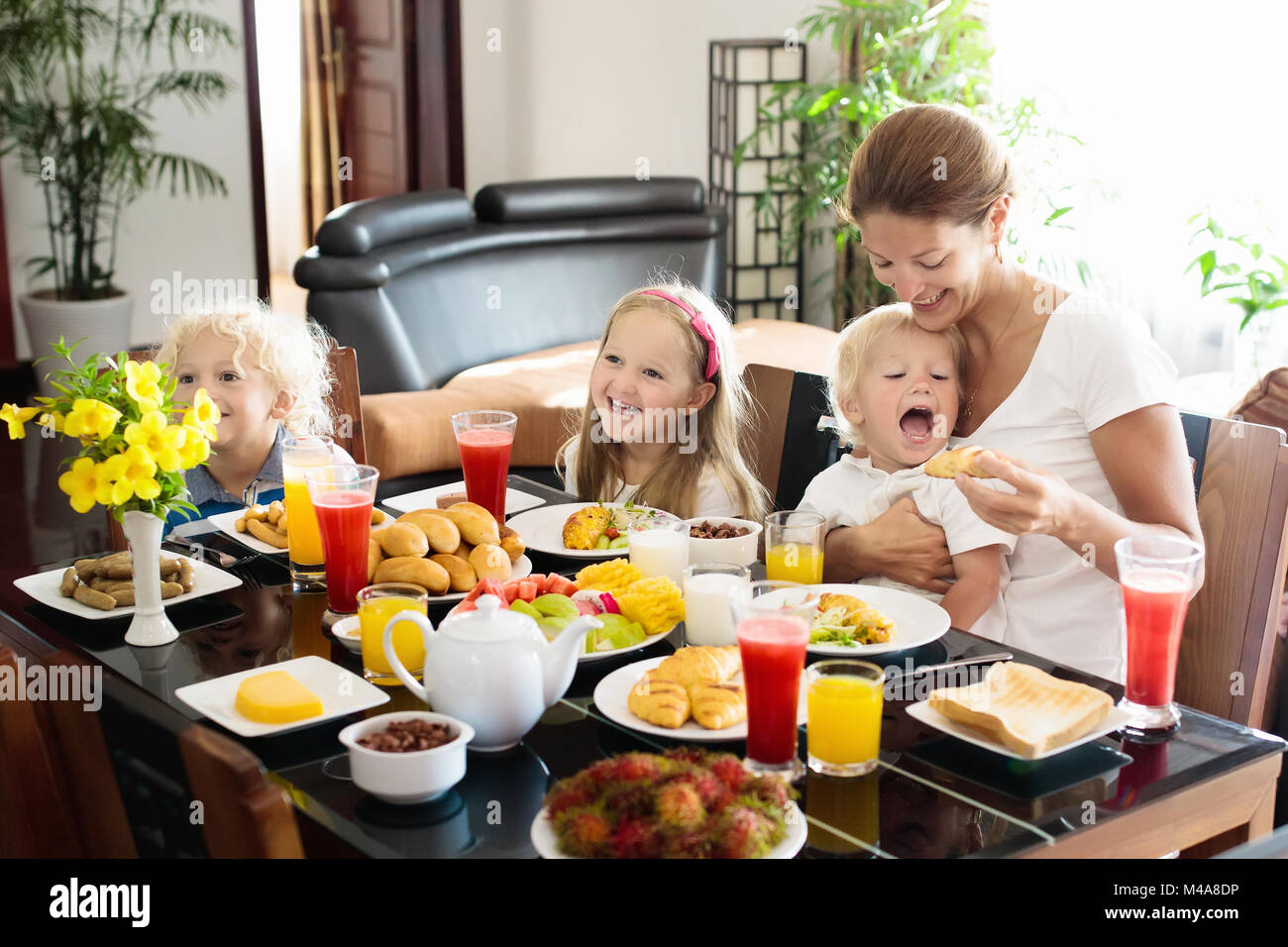 Healthy family breakfast at home. Mother and kids eating tropical fruit ...