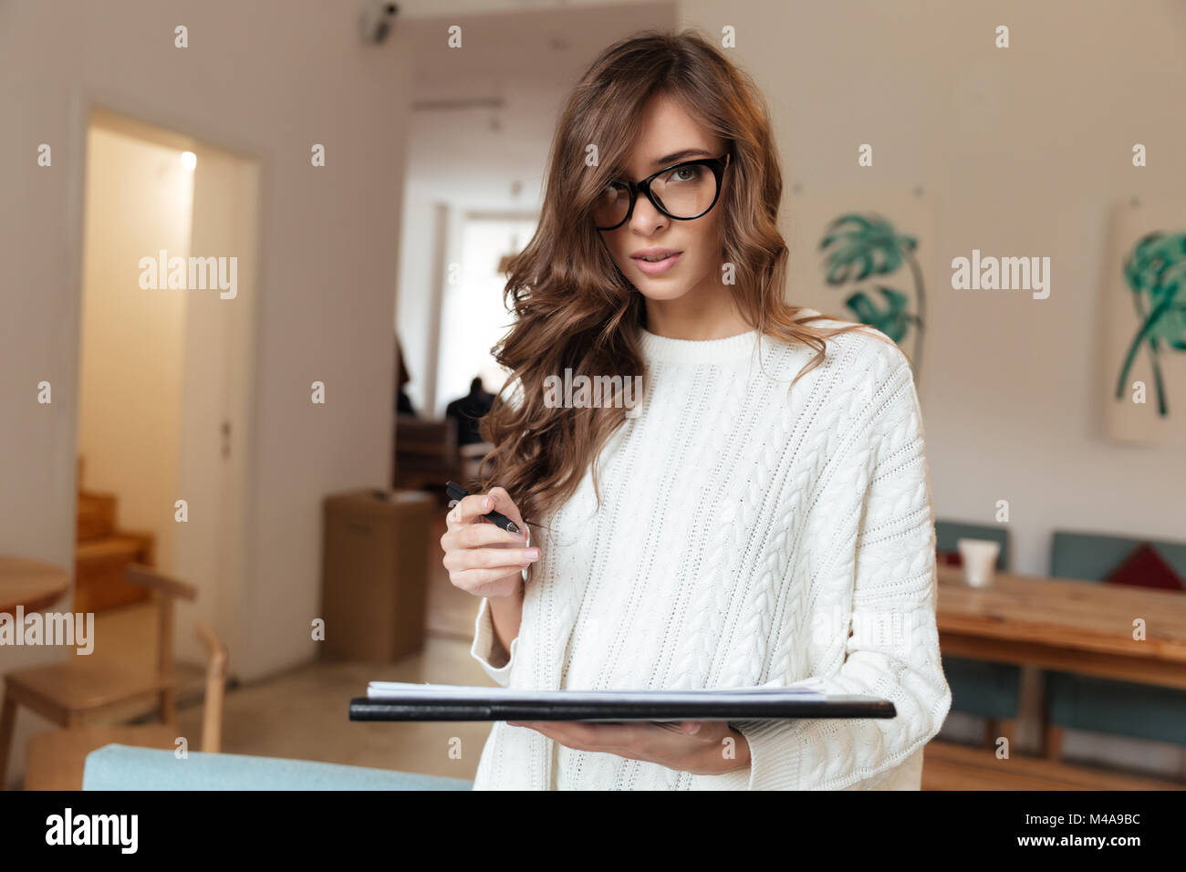 Portrait of a young woman making notes in a notepad while standing ...