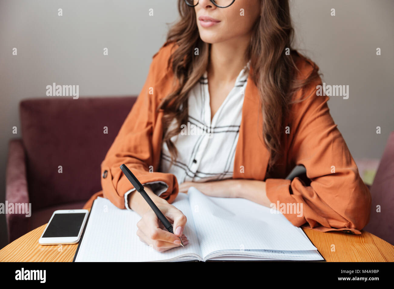 Cropped image of a young woman taking notes in a notepad while sitting ...