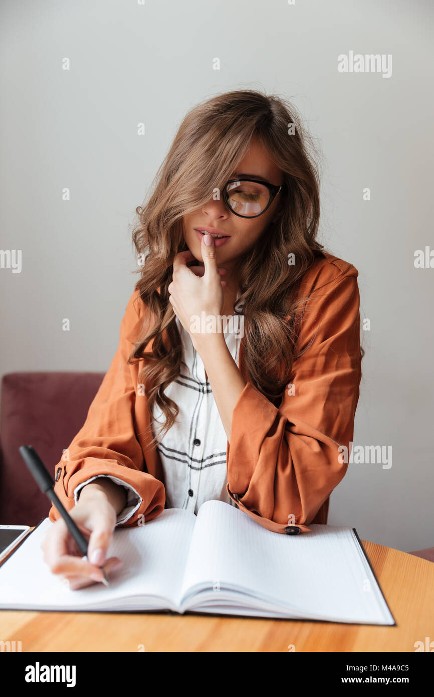 Portrait of an attractive woman taking notes in a notepad while sitting ...