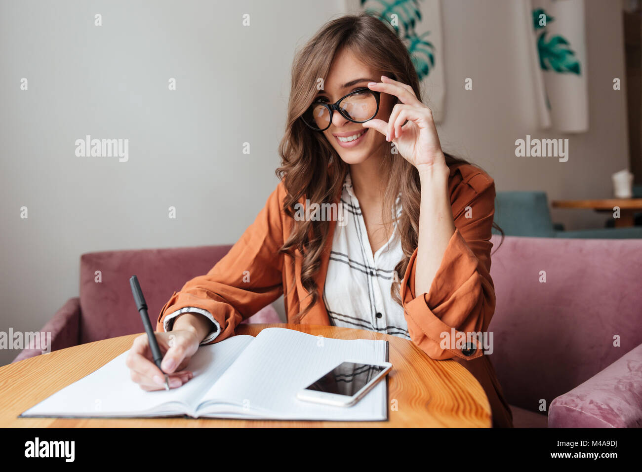 Portrait of a confident woman taking notes in a notepad while sitting ...