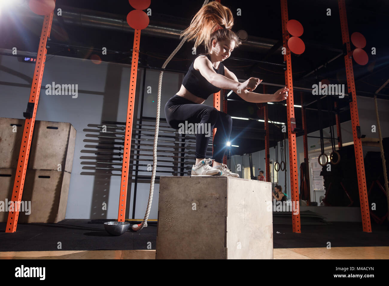 Fit young woman box jumping at a cross fit gym. Female athlete is ...