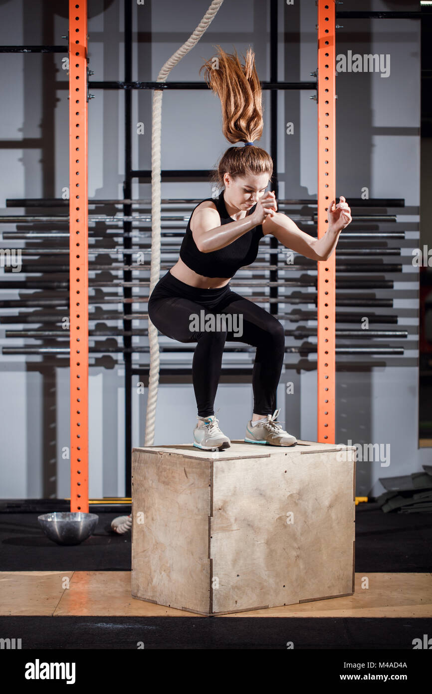 Fit young woman box jumping at a cross fit gym. Female athlete is ...
