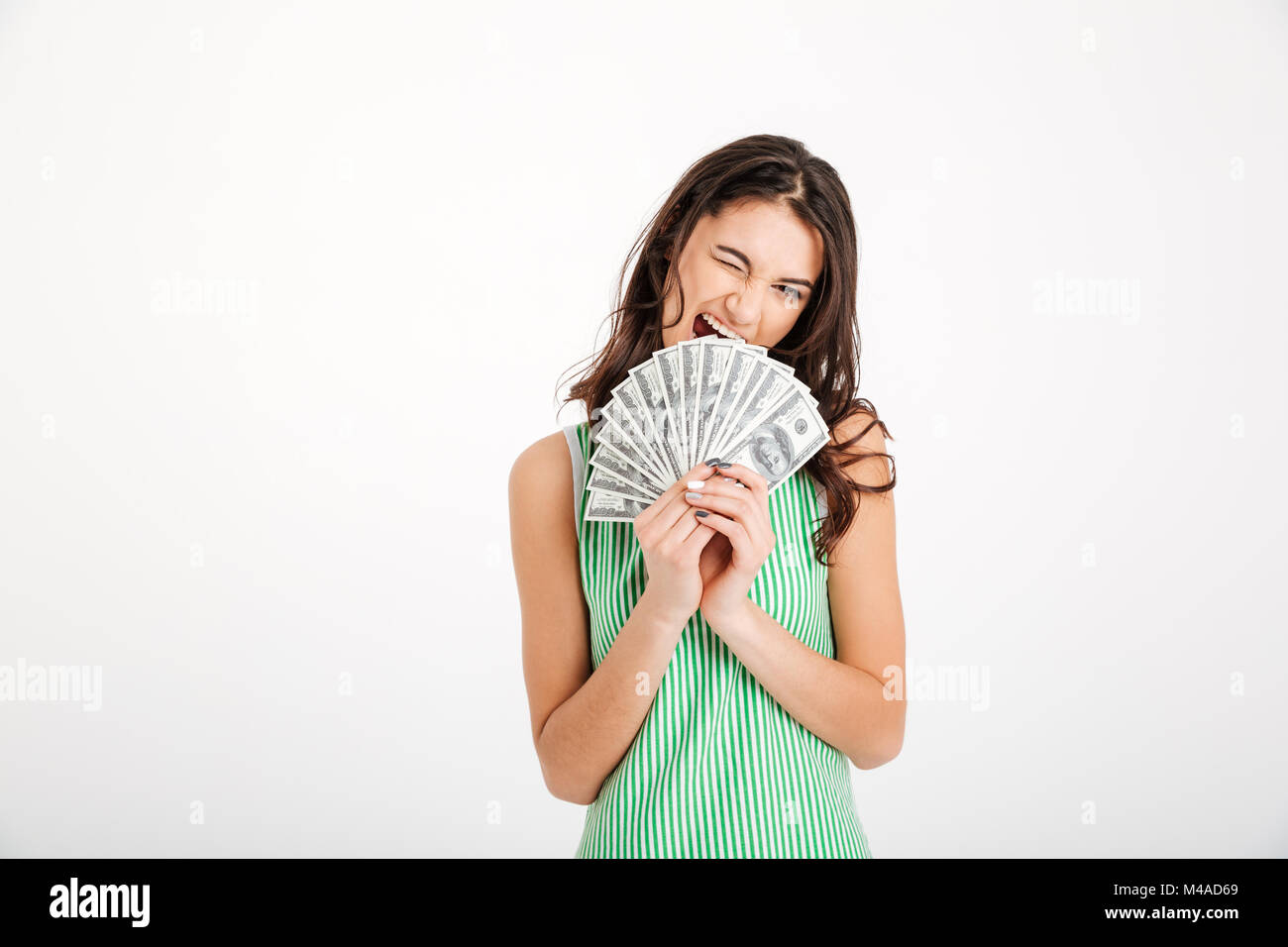 Portrait of a happy girl in dress biting bunch of money banknotes ...