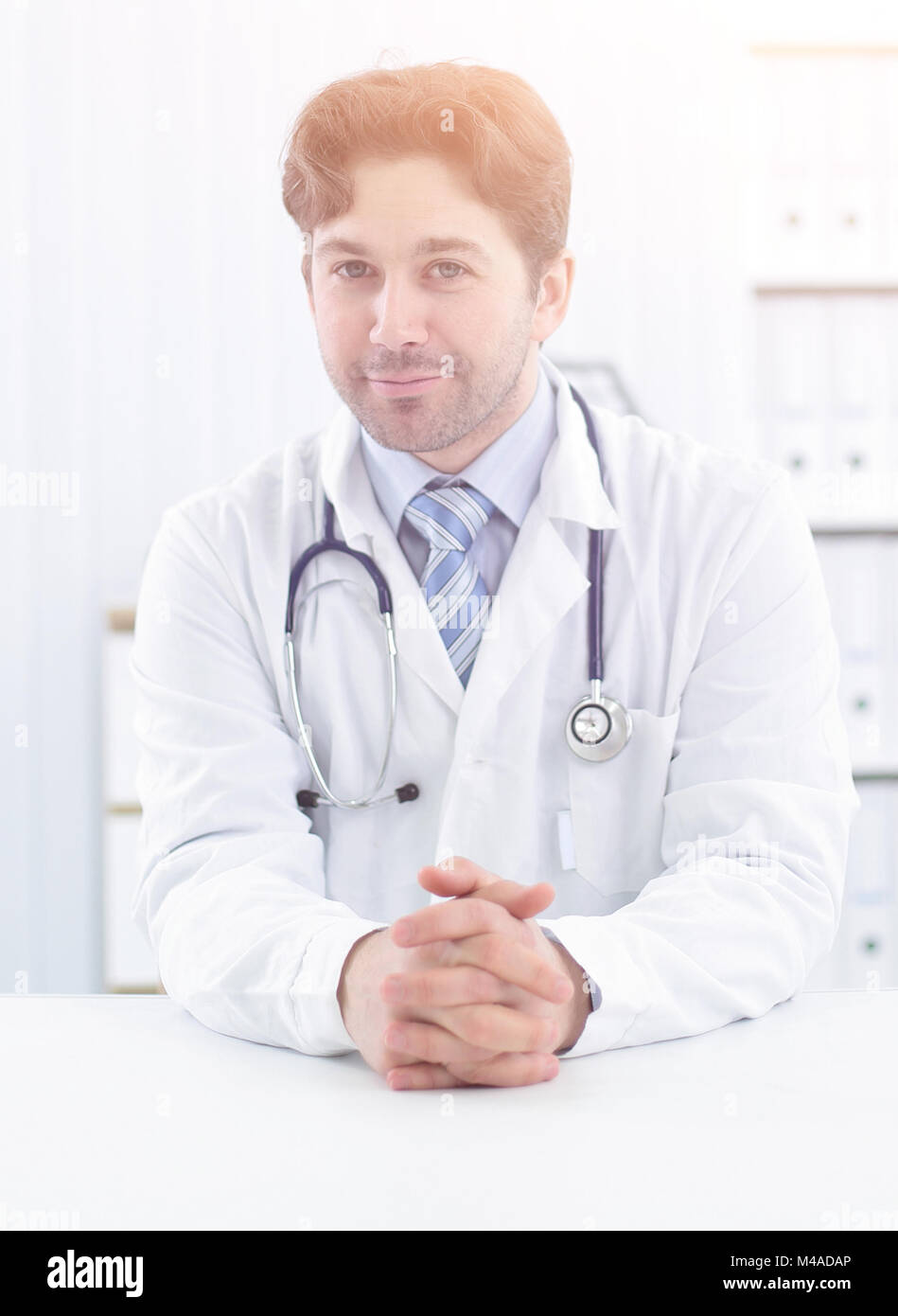 Handsome young doctor in white coat is looking at camera and smiling ...