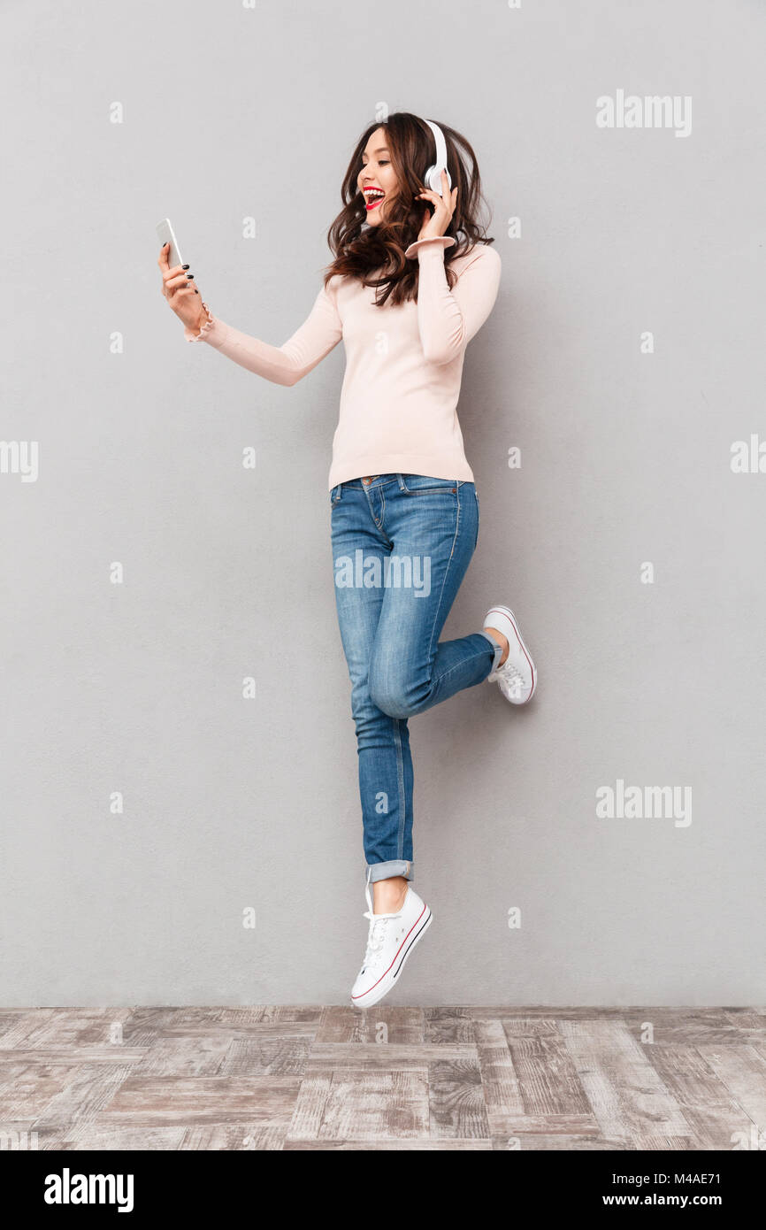 Full-length amazing female music lover wearing white headphones, taking ...