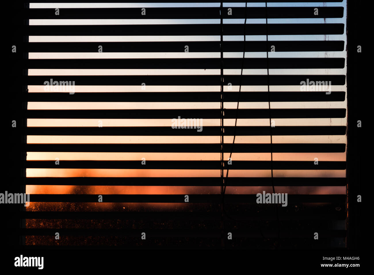 Viewing the sunset through a window with blinds, conveying a ...