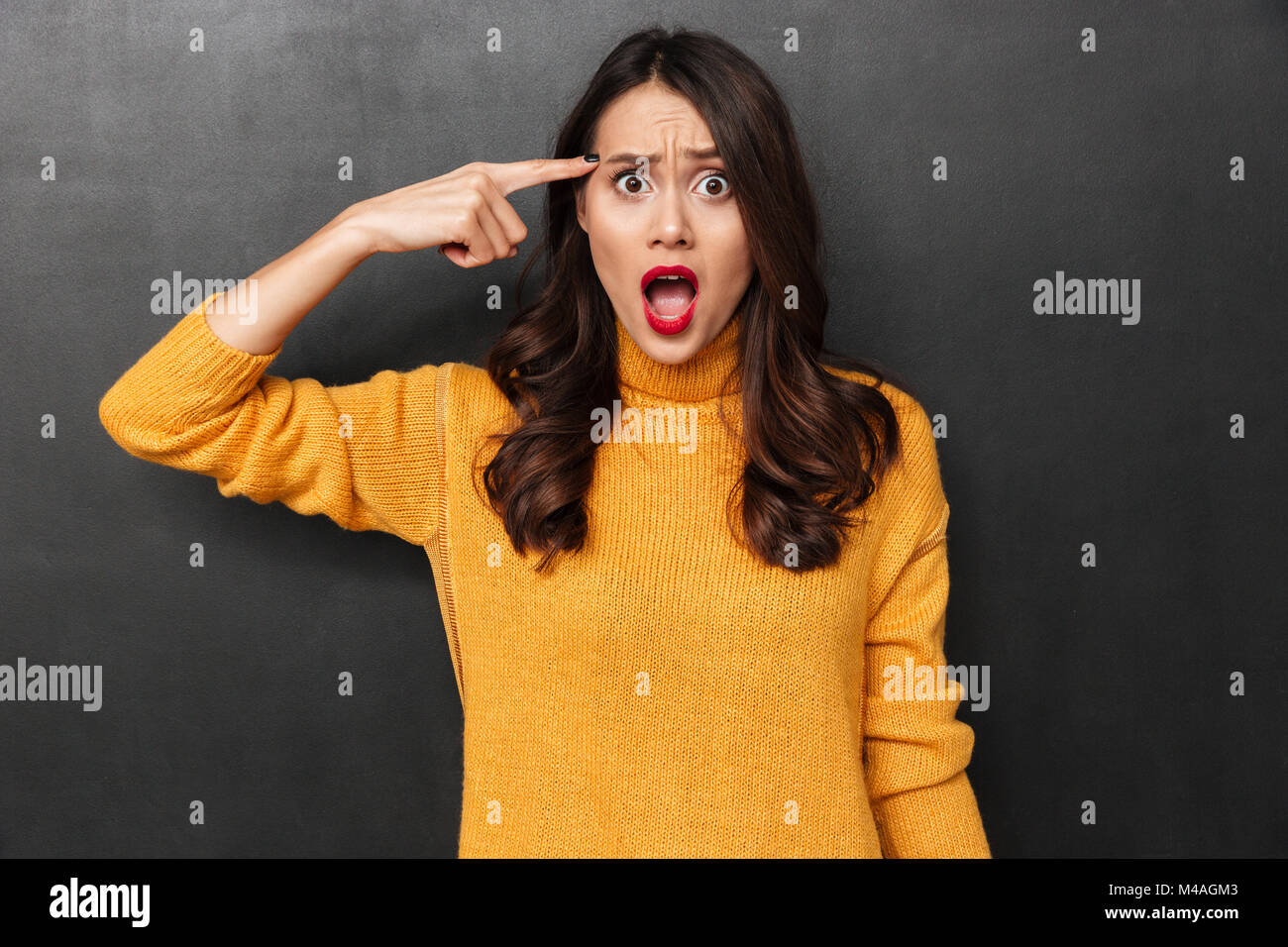 Confused brunette woman in sweater holding finger on temple and looking ...