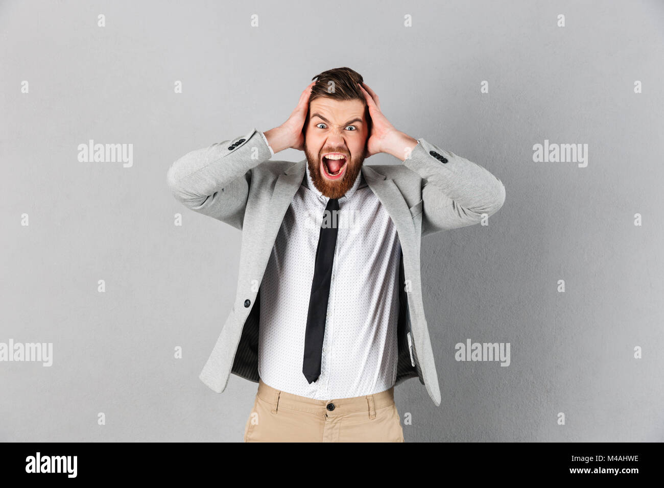 Portrait of an angry businessman dressed in suit covering his ears and ...