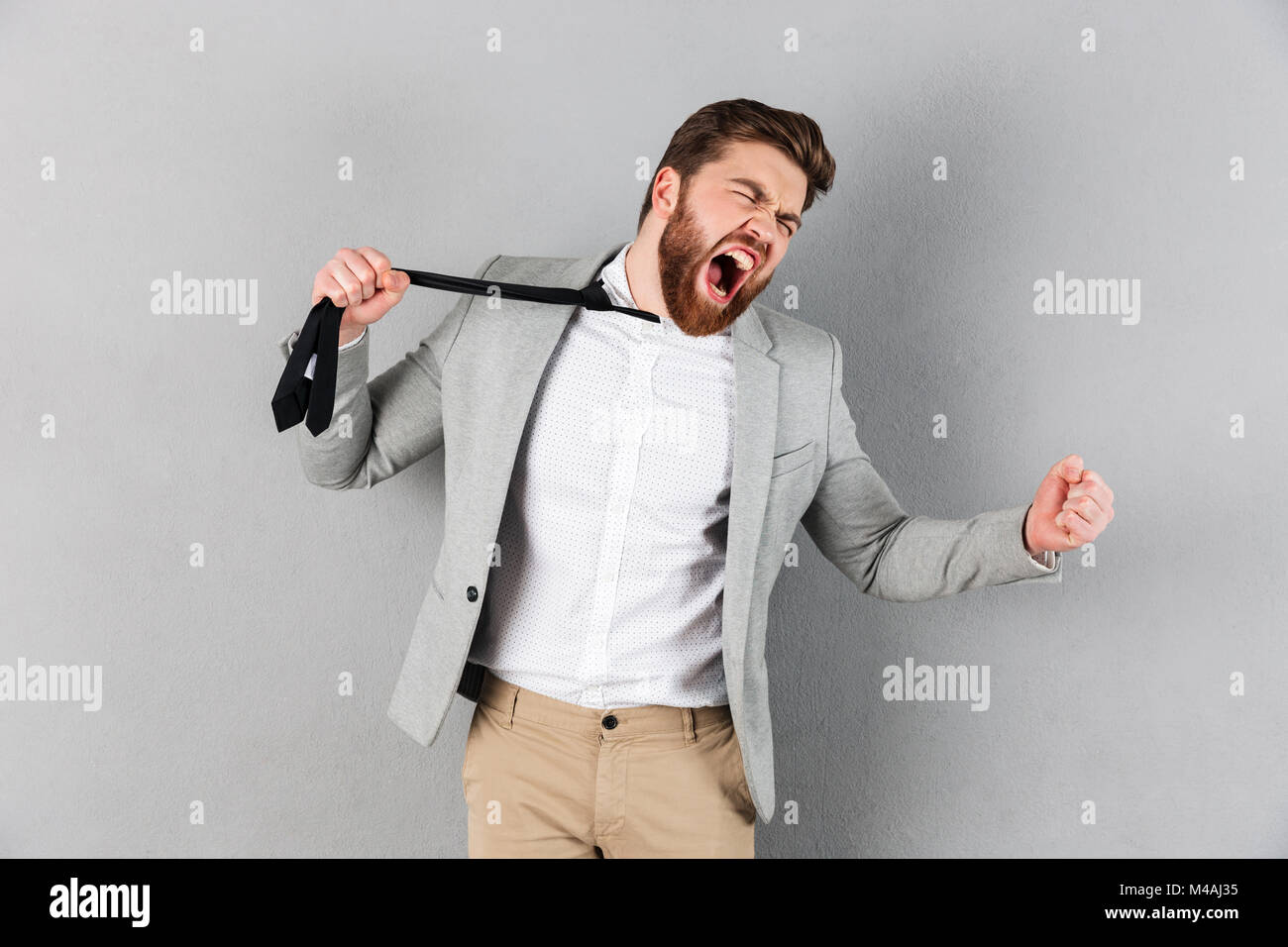 Portrait of an angry businessman dressed in suit screaming and pulling ...