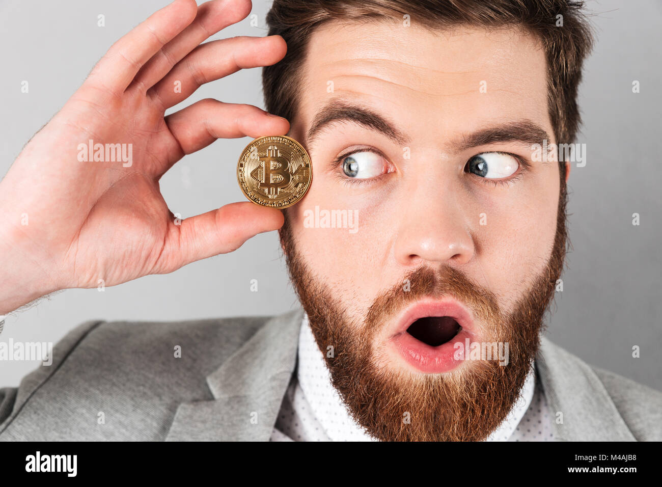 Close up of a curious businessman dressed in suit holding bitcoin at ...