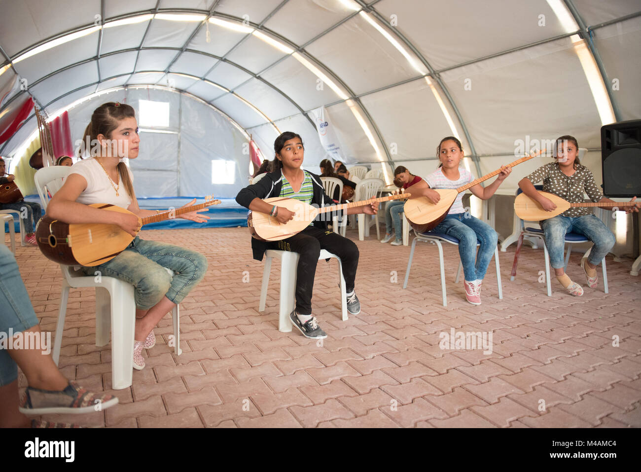 A group of Syrian refugee girls learn to play a string instrument ...