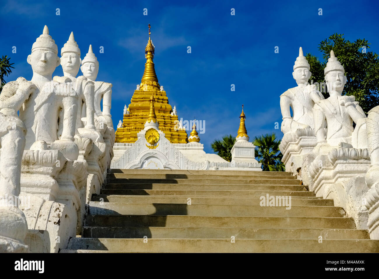 White Buddha statues are flanking the stairs up to the golden Settawya ...