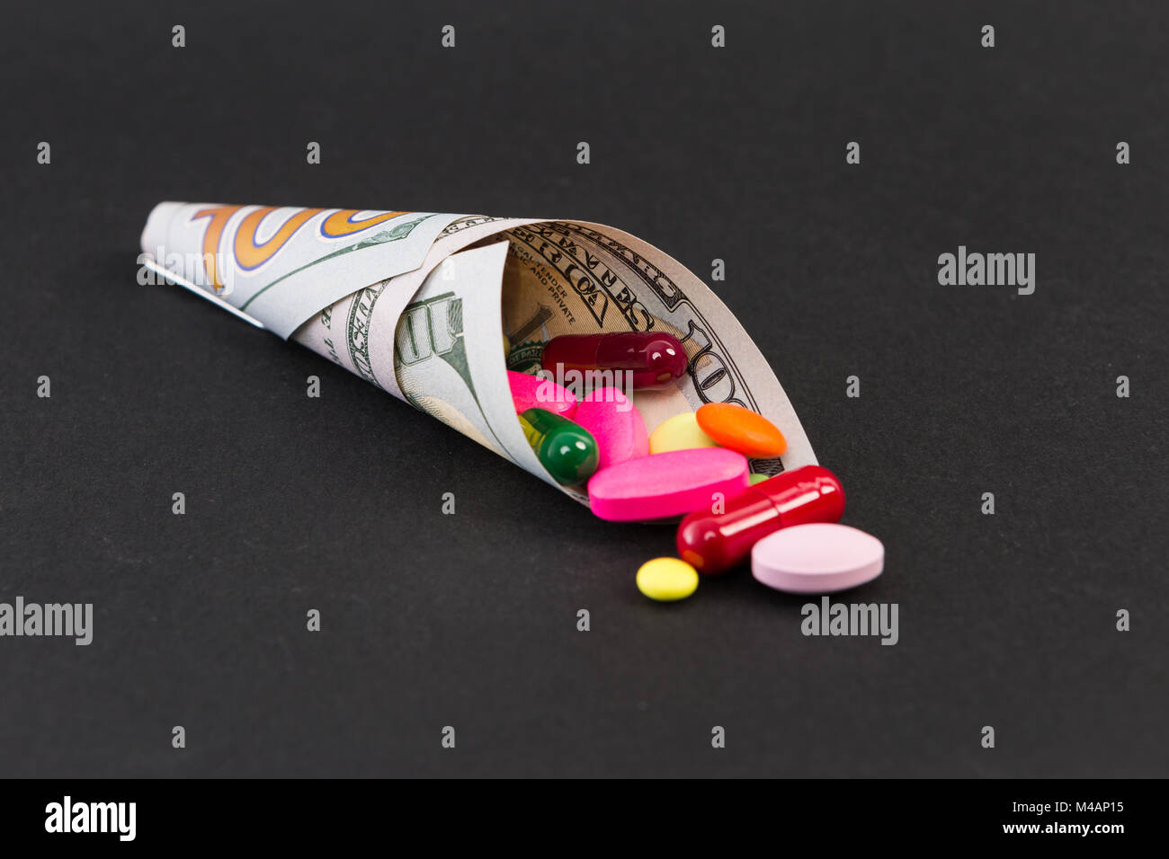 Pills and capsules wrapped in one hundred dollar bill isolated on dark ...