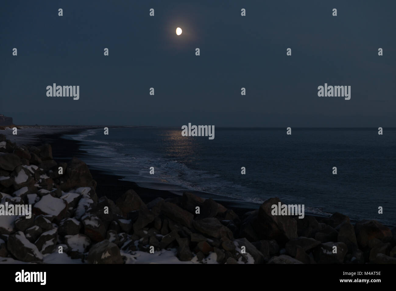Moon reflecting on the ocean along a snowy, rocky beach Stock Photo - Alamy