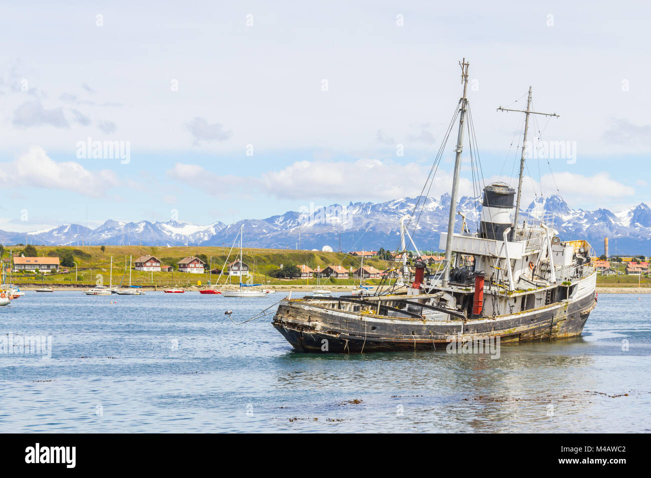 Old boat in Beagle channel with mountains and houses in Ushuaia ...