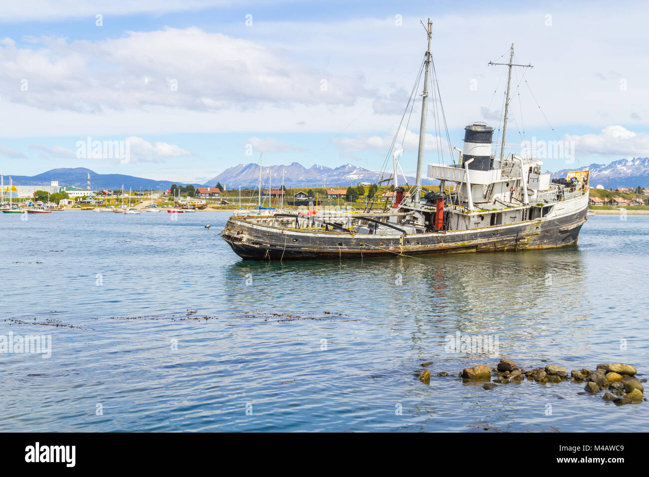 Old boat in Beagle channel with mountains and houses in Ushuaia ...