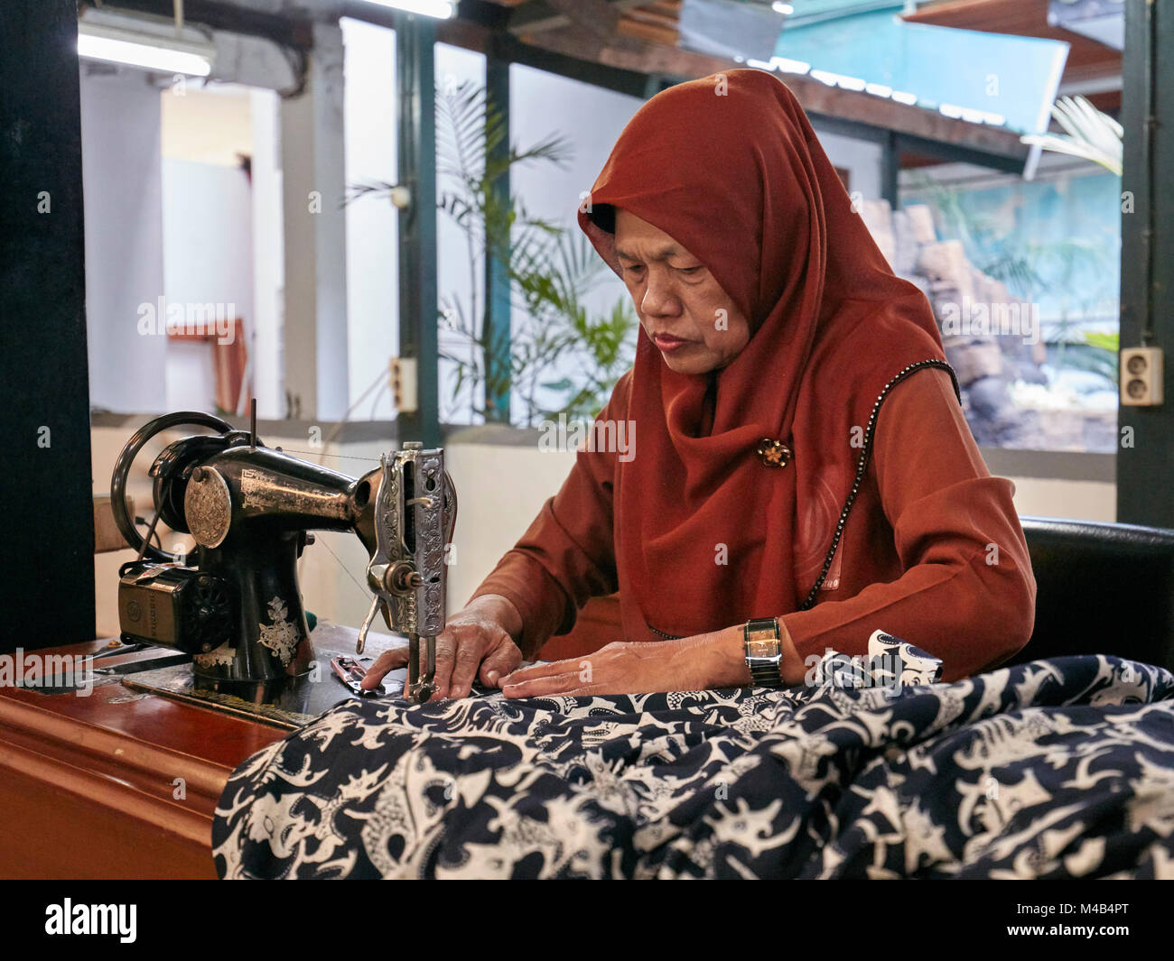 A woman sews a batik shirt using vintage sewing machine. Batik ...